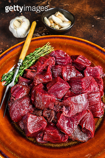 Raw diced elk meat steak for a goulash on a plate. Dark background. Top ...