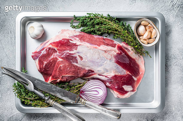 Raw lamb mutton shoulder meat in a baking dish with thyme and garlic ...