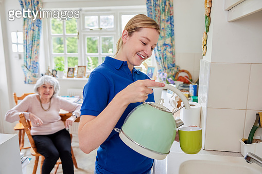 Female Home Help Making Cup Of Tea In Kitchen Whilst Chatting With ...