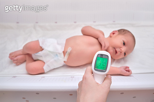 Mom measures the body temperature of a newborn baby with a non-contact ...