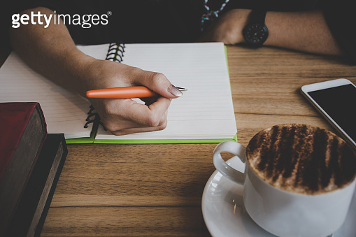 Woman hand with orange pen writing on notebook at coffee shop. Woman ...