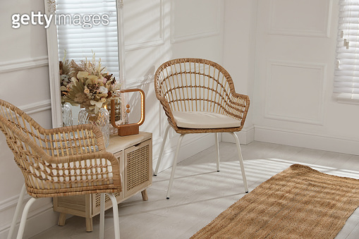 Living room interior with wooden commode, mirror and wicker chairs ...