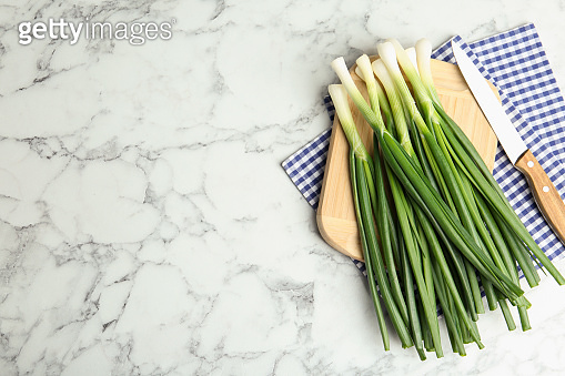 Fresh green spring onions, knife and cutting board on white marble ...