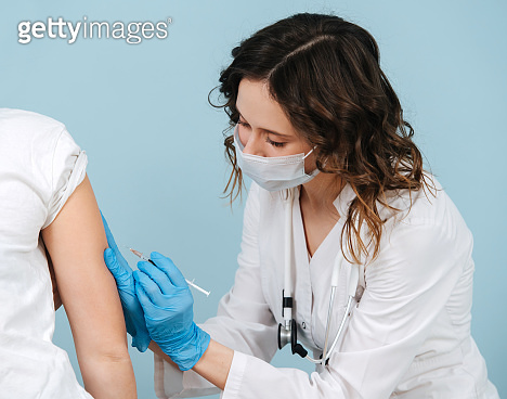 Keen nurse giving shoulder vaccine injection. Over blue background. 이미지 ...