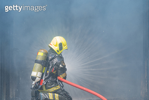 A firefighter or fireman with uniform using water fire hose against hot ...