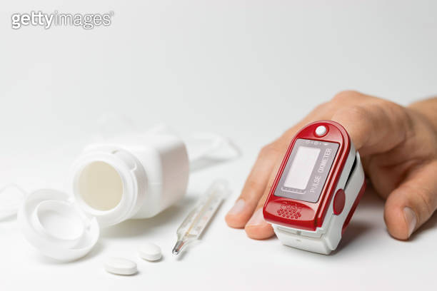 Hand with a portable pulse oximeter on a finger, thermometer and pills ...