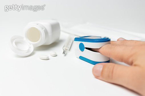 Hand with a portable pulse oximeter on a finger, thermometer and pills ...