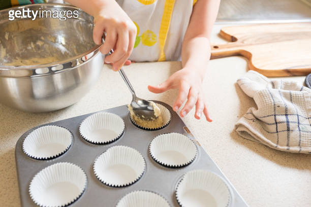 Child's hands spooning cupake mixture into paper pans 이미지 (1344668560 ...