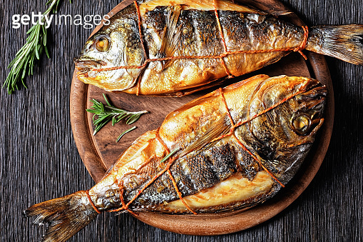 hot smoked gilt-head sea bream, orata fish on a wooden round cutting ...