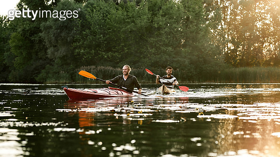 Two male friends looking cheerful while boating together on a lake ...