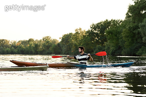 Active young caucasian guy looking concentrated while boating on a lake ...