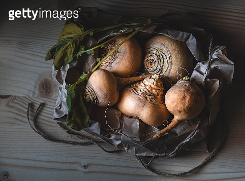 fresh turnips in a crumpled paper bag on a light table. turnip sprigs ...