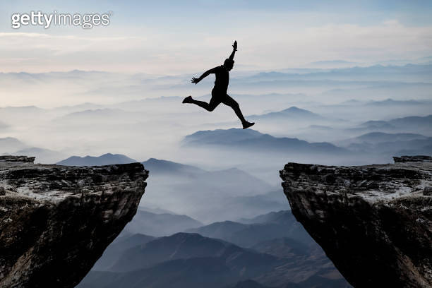 Silhouette of man jumping from one cliff to another cliff with ...
