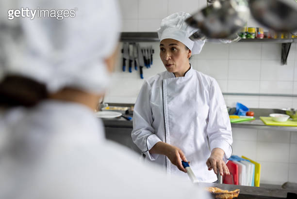 Head chef explaining to a group of cooks how to prepare a plate ...