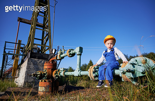 Adorable little boy sitting on pump jack pipe in oil field. 이미지 ...
