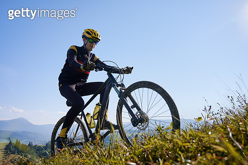 Joyful male cyclist riding bicycle uphill under blue sky. 이미지 ...