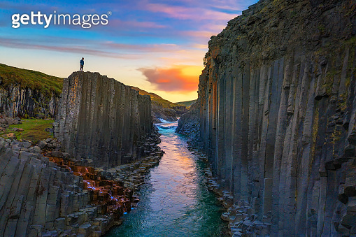 Hiker standing at the top of Studlagil Canyon in Iceland at sunset 이미지 ...