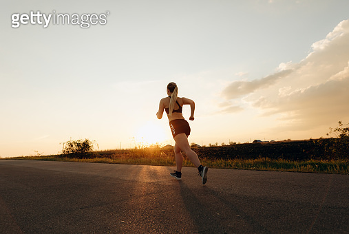 Young sporty girl running on a road at sunset. Lifestyle sports ...