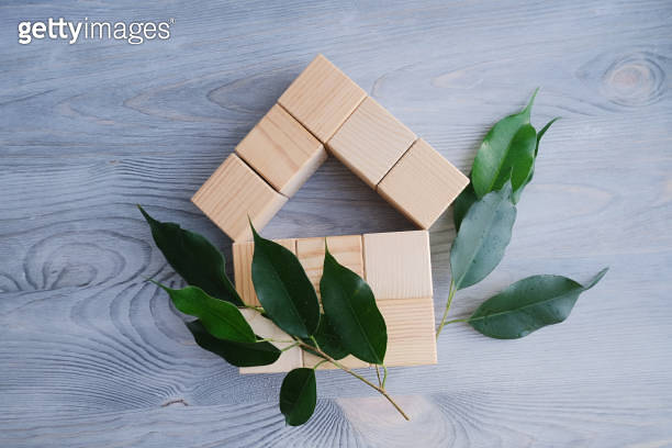 House made of wooden cubes with green branches with leaves on a wooden ...