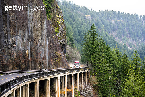 Red big rig semi truck with flat bed semi trailer running on the wet ...