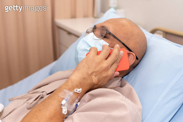Cancer patient man lies on a hospital bed wearing a mask and talking on ...