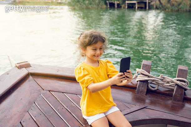 Cute little girl sailing in a rowboat at sunset, plying with a ...