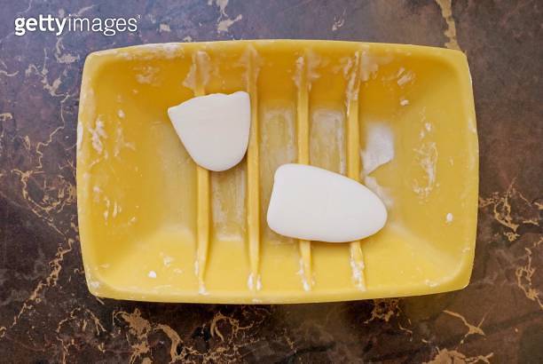 Broken remains of a bar of soap in a soap scum filled soap dish on top ...