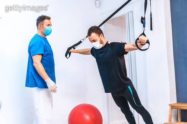 Physiotherapist with mask and a patient doing stretches upside down ...