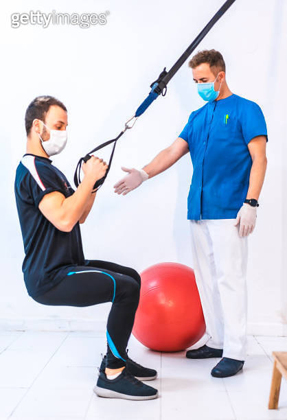Physiotherapist in blue gown and a patient with rubber arm exercises ...