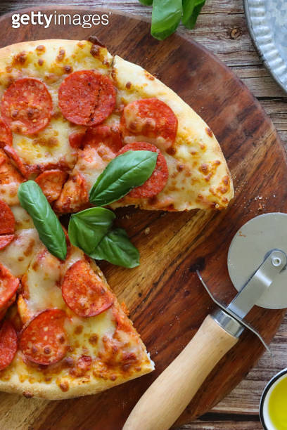 Full frame image of sliced pepperoni pizza on round wooden chopping ...