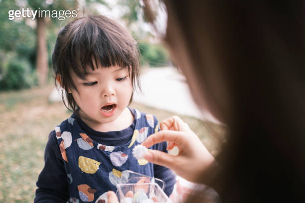 Cute Chinese girl eating sweets in the park 이미지 (1293388058) - 게티이미지뱅크