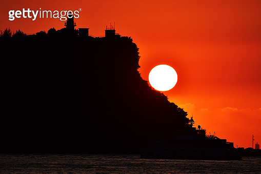 The sun falling down behind mountain and beacon in red sky at sunset ...