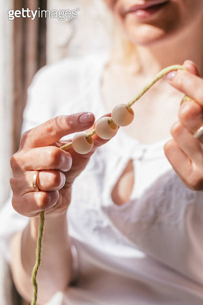 Close-up of a woman's hands stringing wooden beads on cotton thread for ...