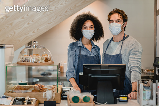 Two cafeteria staff standing at cafe counter in medical masks against ...