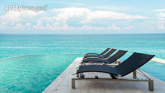Luxury poolside with sun beds and deck chairs over blue sea. Tranquil ...