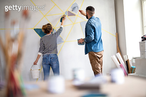 Rear view of couple painting wall indoors at home, relocation and diy ...