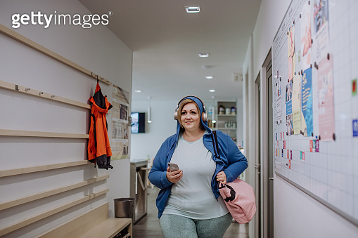 Happy overweight woman in sports clothes indoors in corridor on the way ...