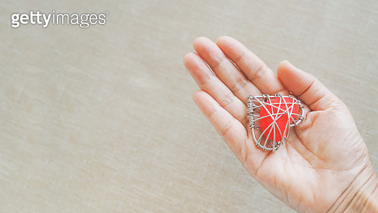 red heart in wire mesh on human's hand with blurred light brown ...