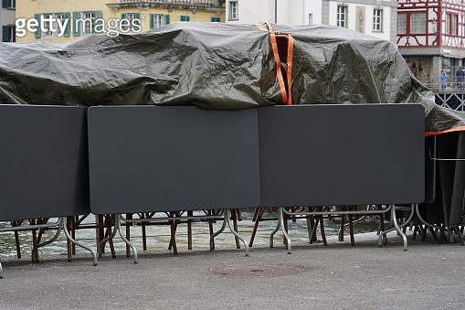 Stapled chairs and tables of a closed terrace restaurant partly covered ...