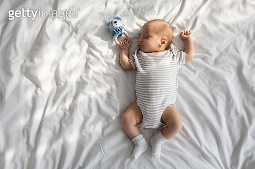 Adorable Little Newborn Baby Sleeping On Bed With Rattle Toy In Hand ...