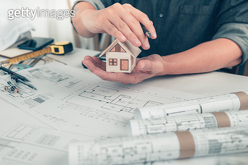 Architect engineer hands hold and protect mini house model on blueprint. Protect House, cost ...