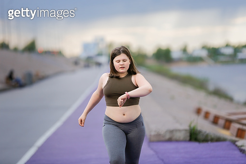 European Teenage Girl Overweight On Jog On Treadmill Along Embankment