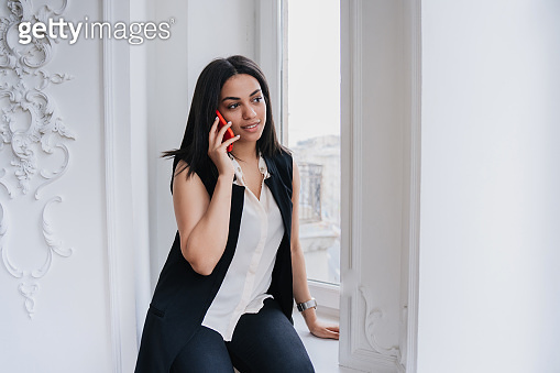 African American smiley young woman sitting on windowsill making call ...