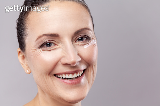 Woman with perfect face skin and cosmetic cream near eyes, looking at ...