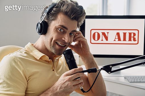 Handsome young man using microphone while recording podcast in studio ...