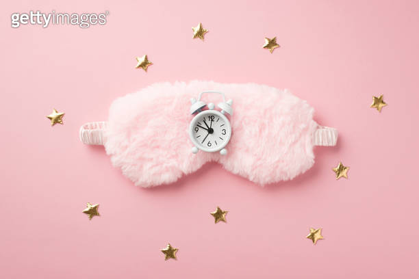 Top view photo of white alarm clock on pink fluffy sleeping mask and ...