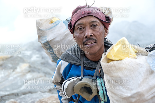 Miner man carrying heavy bags of sulfur on his shoulder in volcano ...