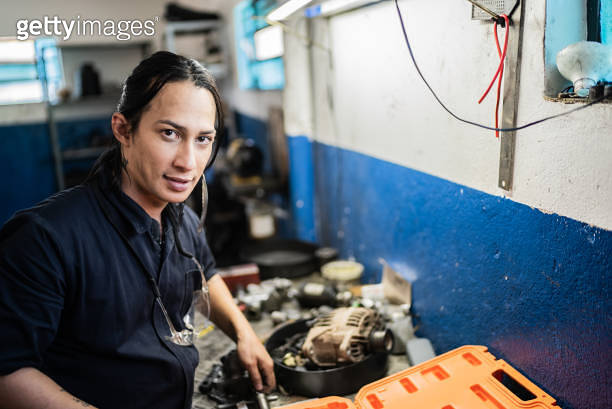 Portrait of Non-Binary person repairing a car in auto repair shop ...