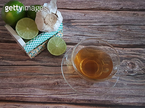 Lemon garlic tea in a clear glass cup with green lemons, a garlic bulb ...