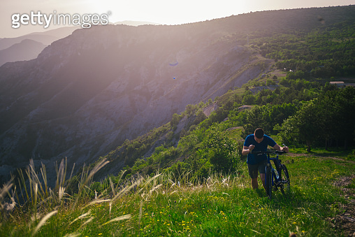Perspective of a fit mountain biker pushing his bike uphill with ...
